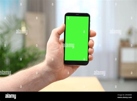Man holding smartphone with green screen indoors, closeup. Gadget display with chroma key ...