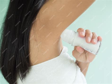 Premium Photo | Woman applying deodorant roll on under armpit after shower on green wall ...