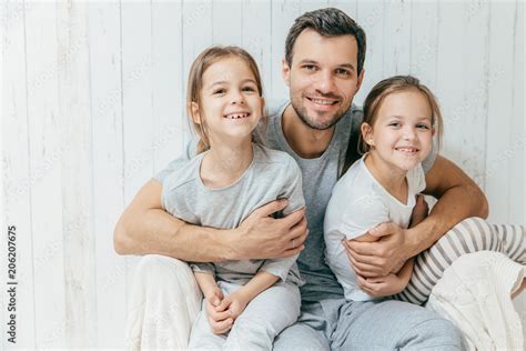 Portrait of happy young father embraces his two daughters, loves them ...