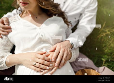 Pregnant woman and man posing at summer park. Close up of human hands holding pregnant belly ...