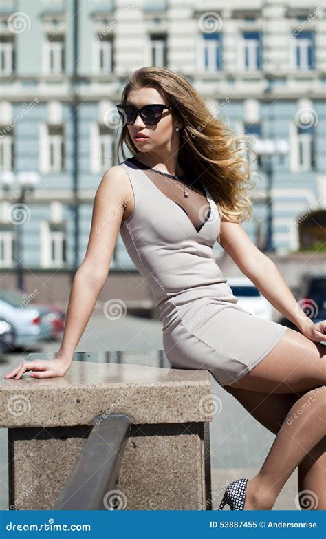 Молодая красивая женщина в бежевом коротком платье представляя Outdoors ...