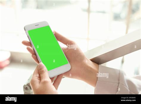 Chroma key compositing. Woman holding smartphone with green screen indoors, closeup. Mockup for ...