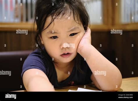 A close up of a cute young Asian girl with an expression of worry and upset on her face, resting ...