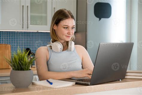 mujer joven feliz trabajando en una computadora portátil en la cocina ...